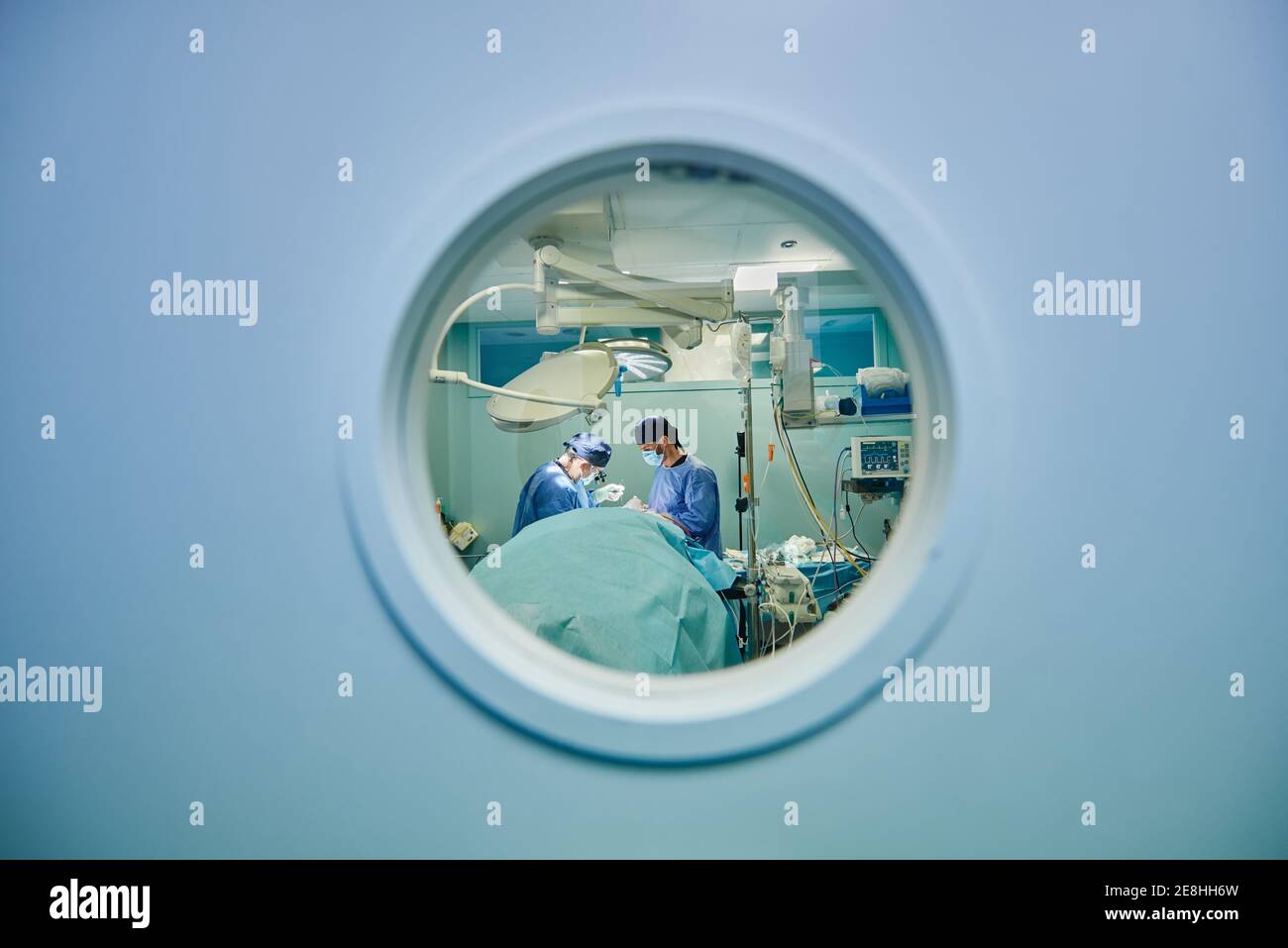 Through round window of unrecognizable doctors in uniforms and masks ...