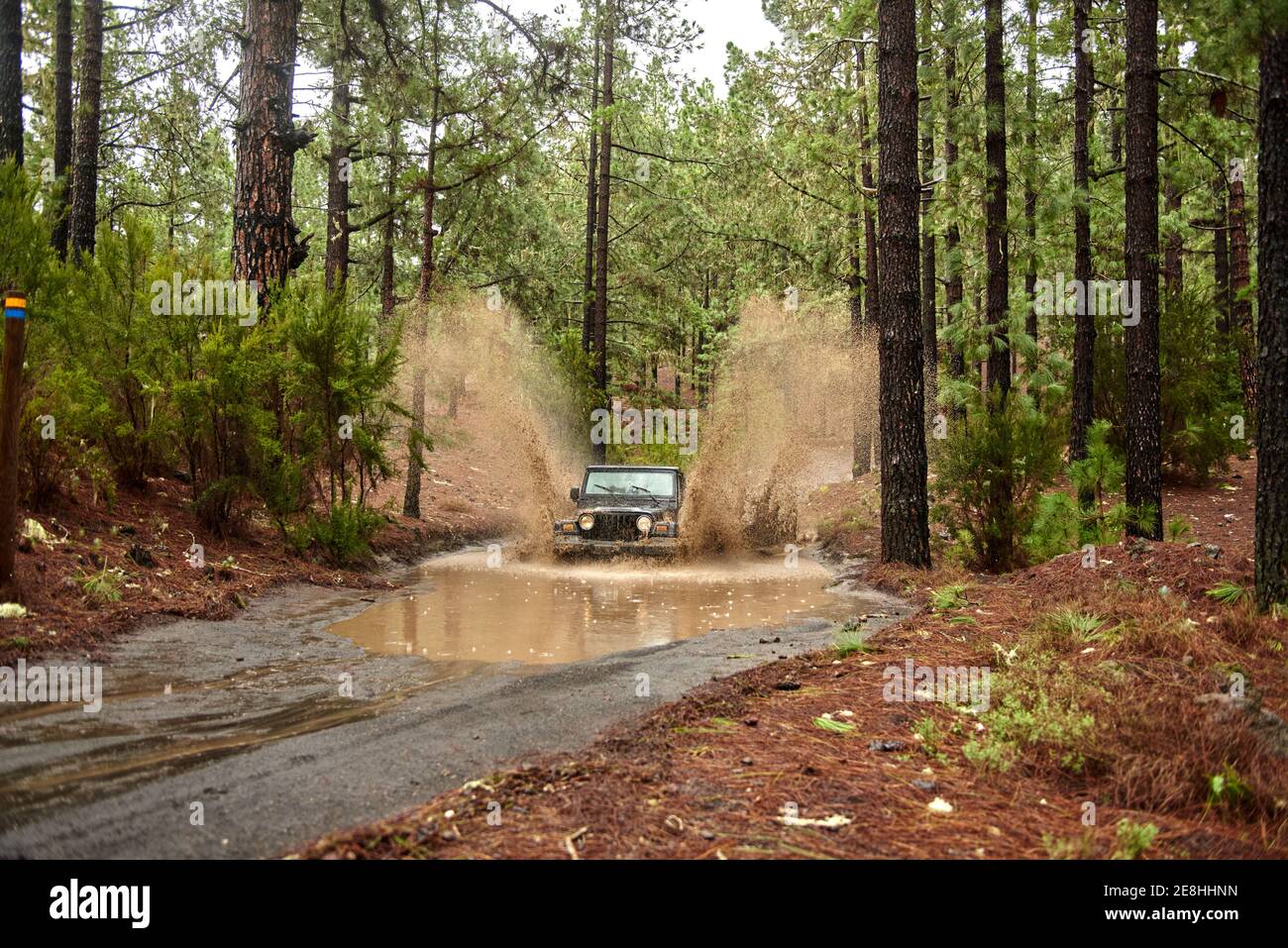 Modern off roader car driving through muddy puddle on rural dirt road ...