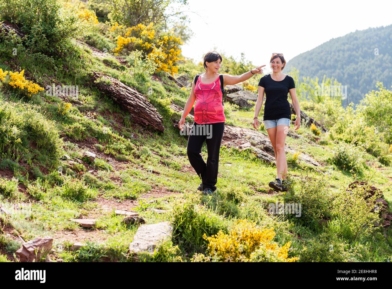 Pregnant Woman and female friend walking along trail in mountainous ...