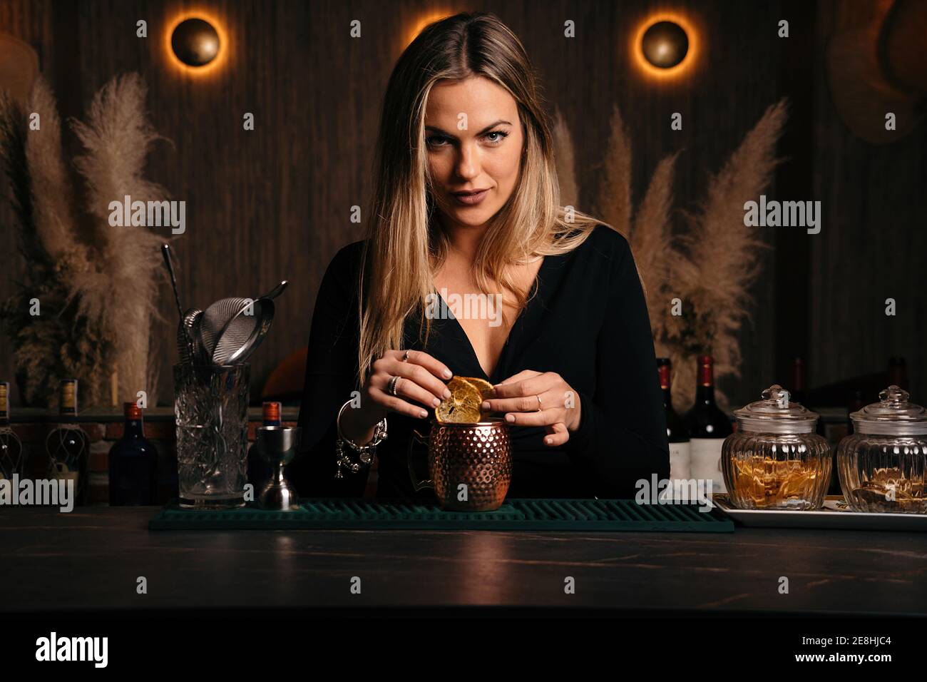 Self assured attractive young female barkeeper with long blond hair in ...