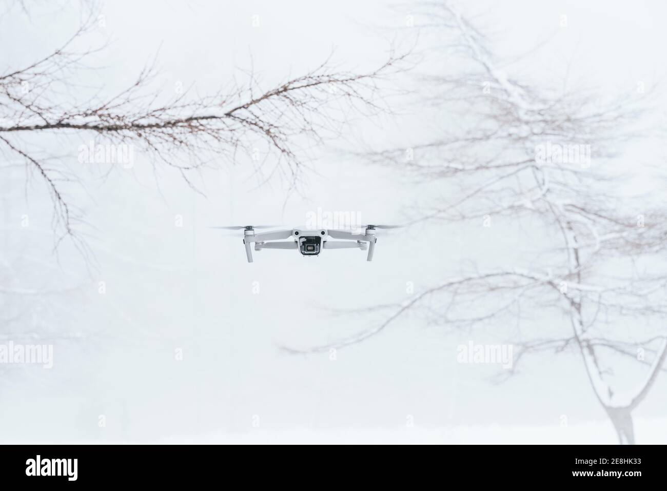 Contemporary white UAV flying over snowy glade in frozen winter woods ...