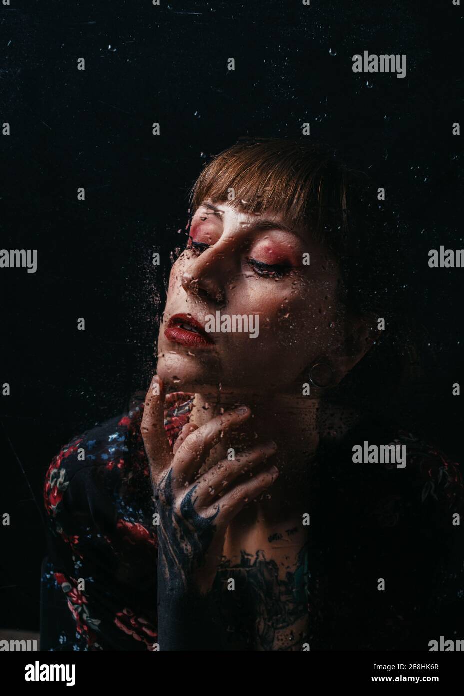 Unemotional female with arm tattoo standing behind translucent glass ...