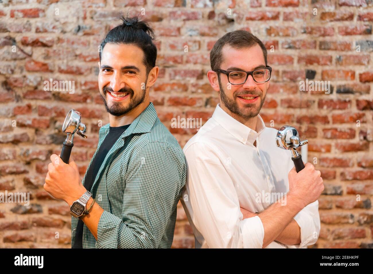 Side view of cheerful male baristas with portafilters standing back to ...