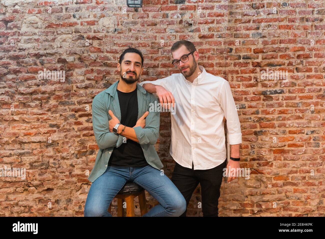 Smiling male baristas looking at camera on background of shabby brick ...