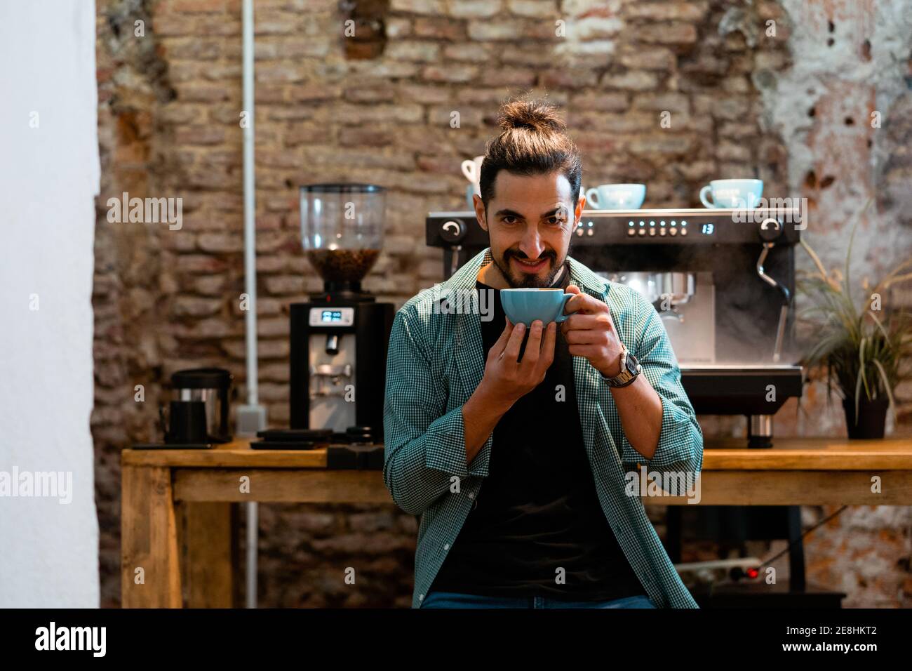 Smiling male barista sitting in cafe and smelling aromatic hot drink ...