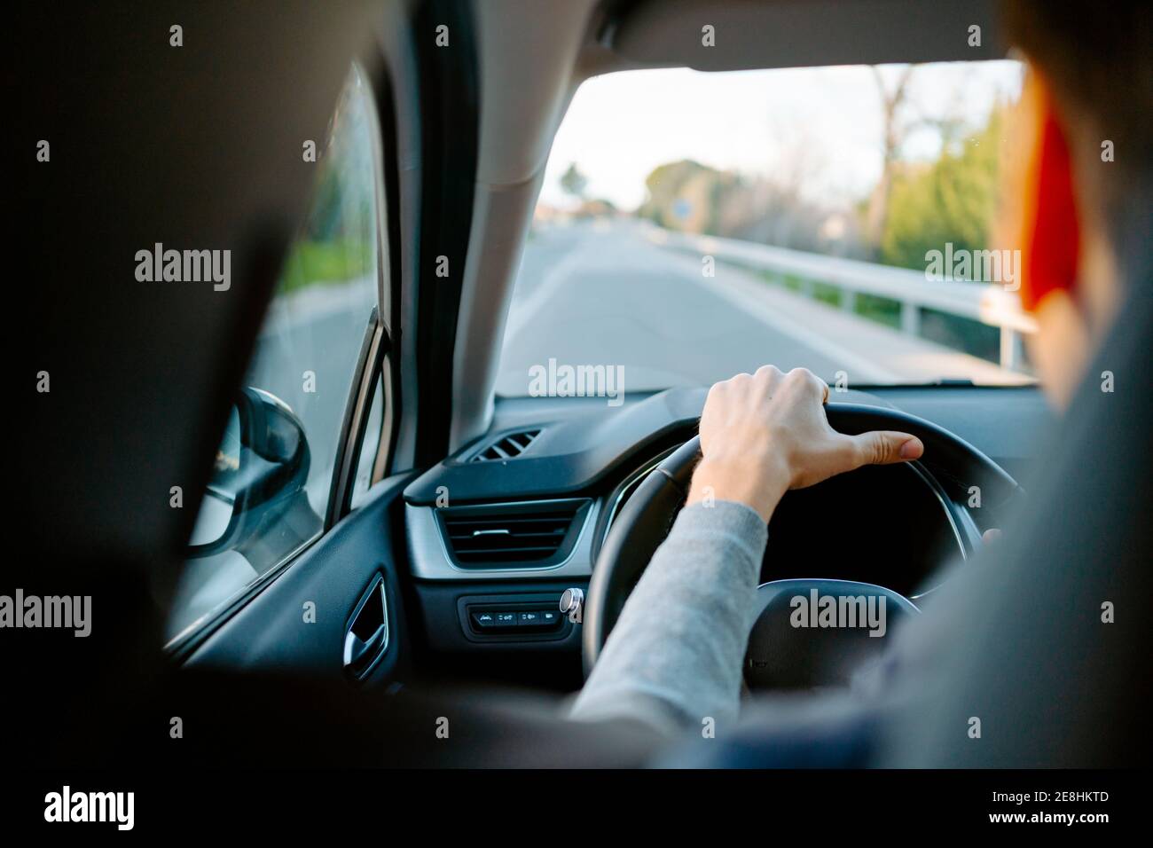 Back view of crop unrecognizable male driving a modern car on sunny day ...