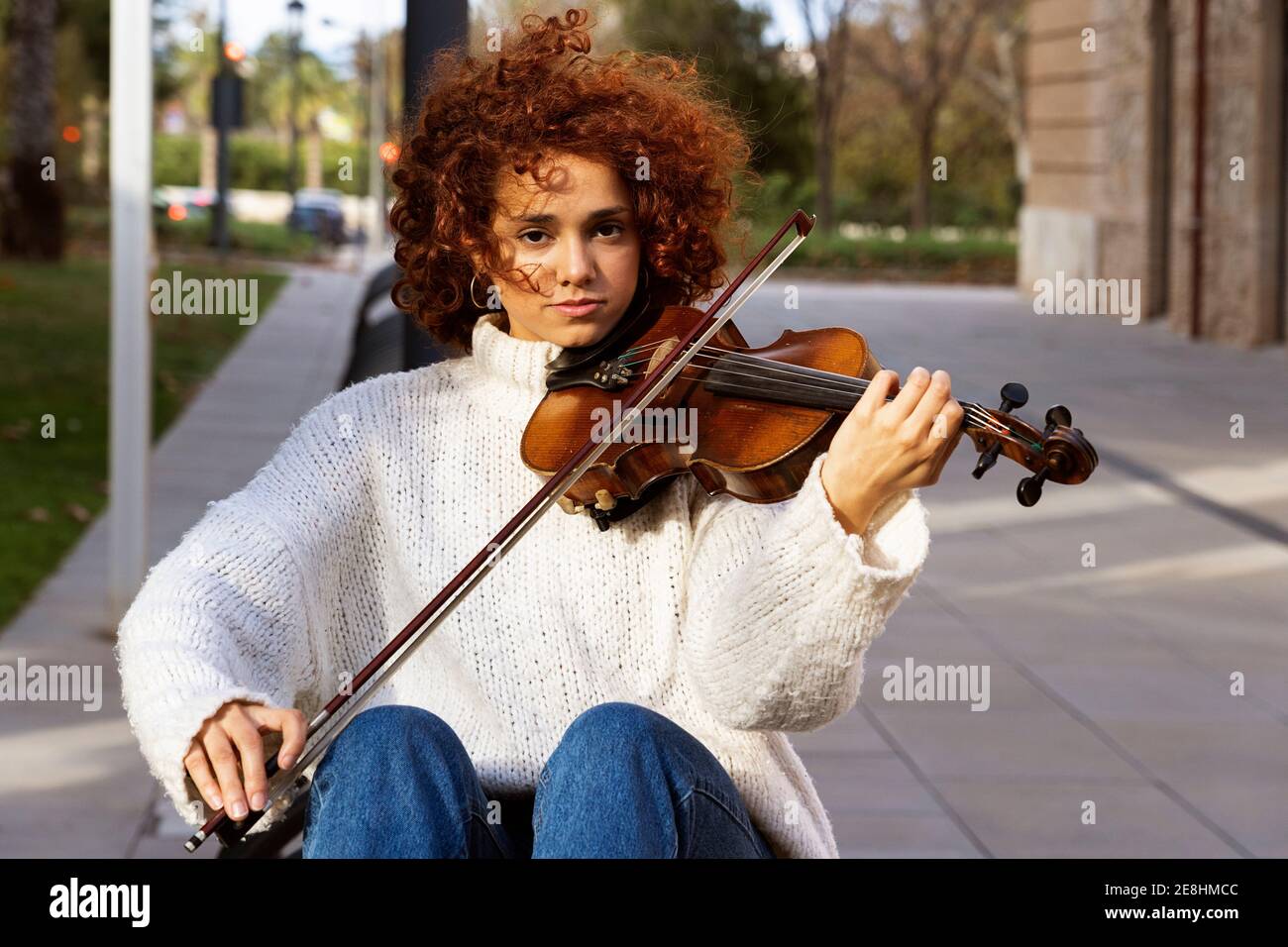 Young pretty female musician in casual wear playing violin and looking ...