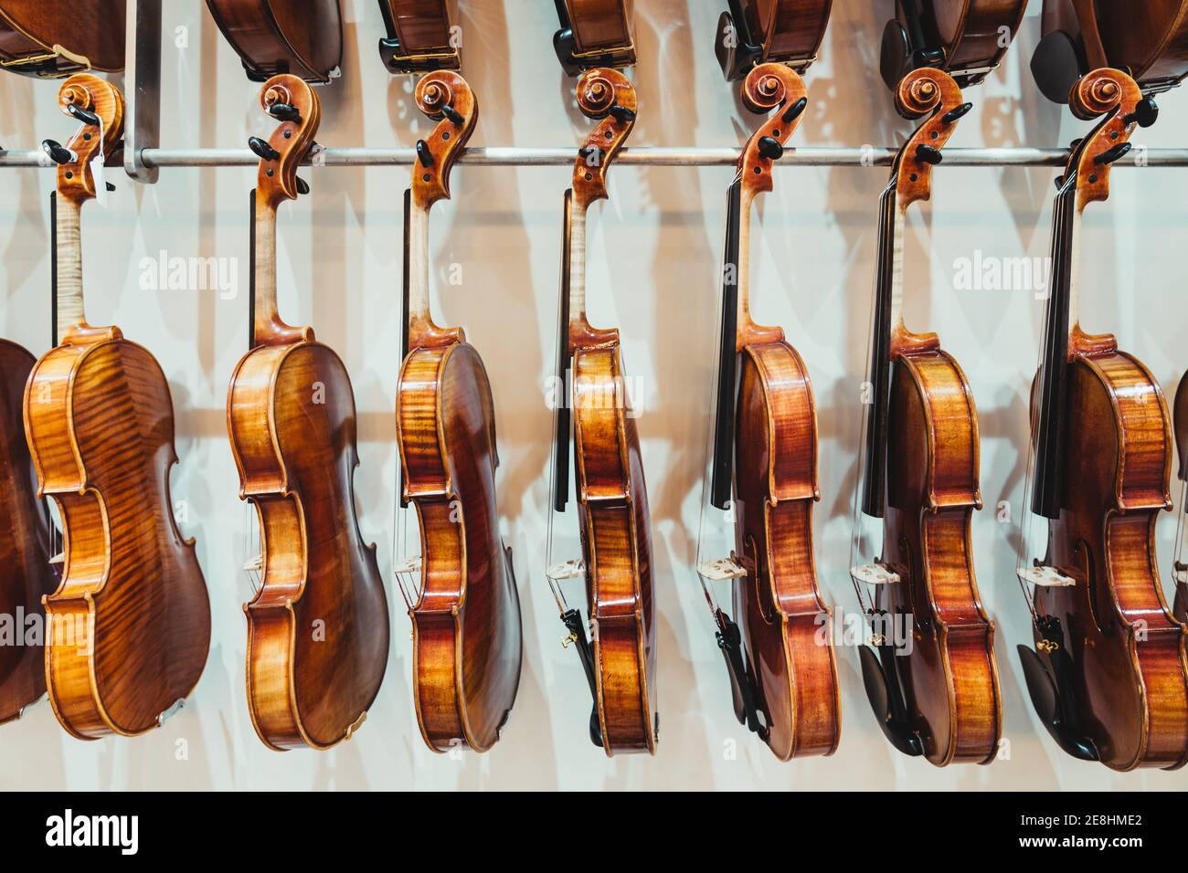 Collection of modern acoustic violins hanging on rack against white ...