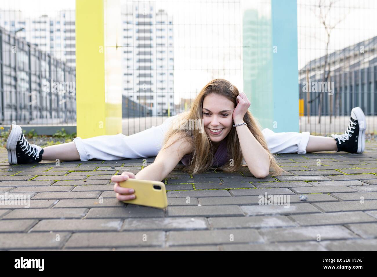 Full body happy fit female doing splits on paved sidewalk and taking ...