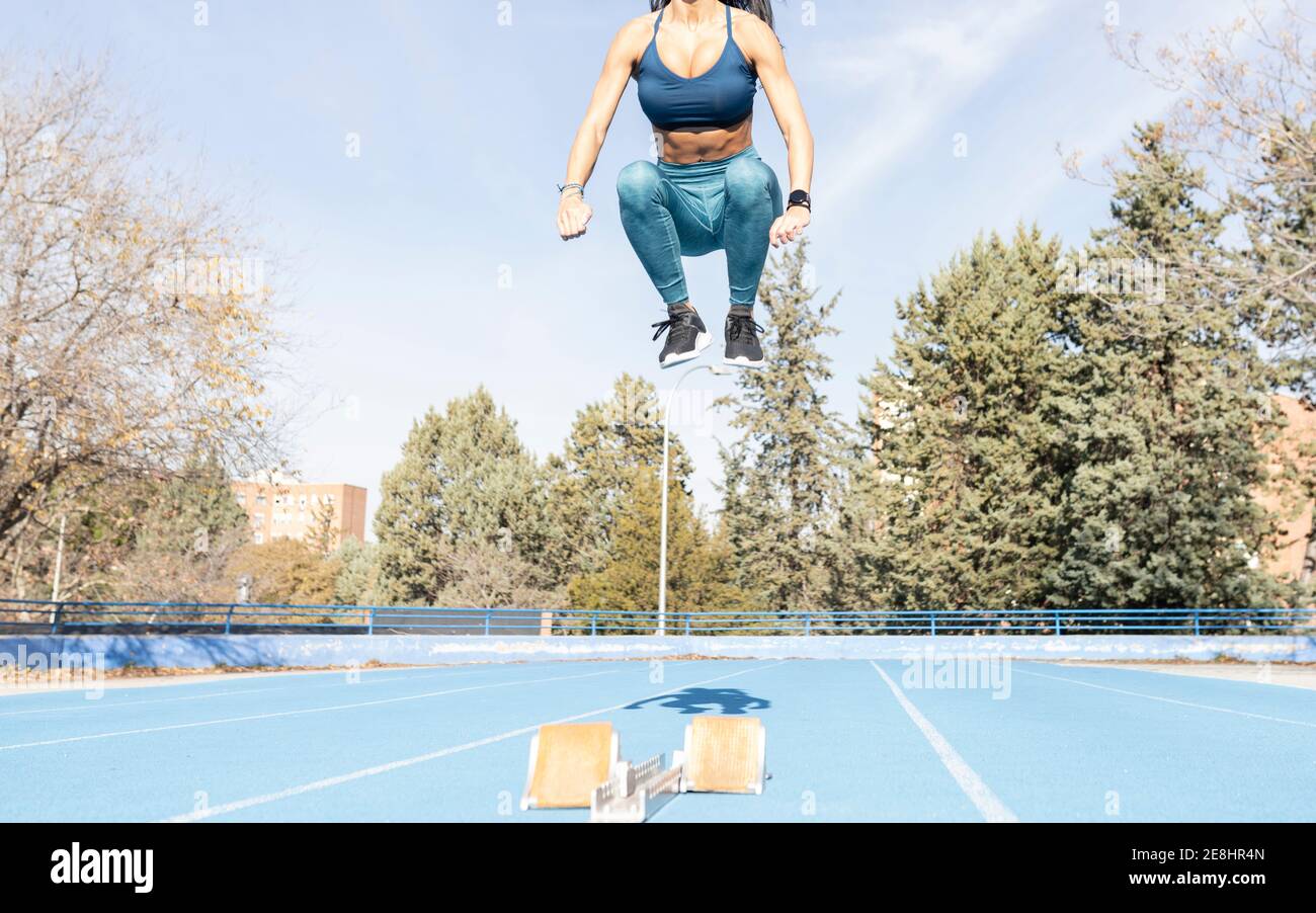 Determined female runner jumping above track with starting blocks while ...