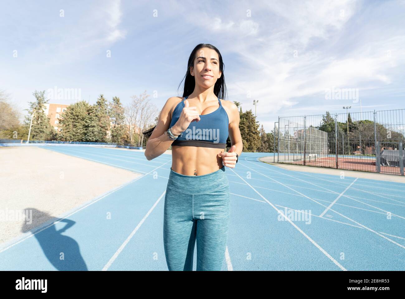 Content muscular sportsWoman running along track at stadium while ...