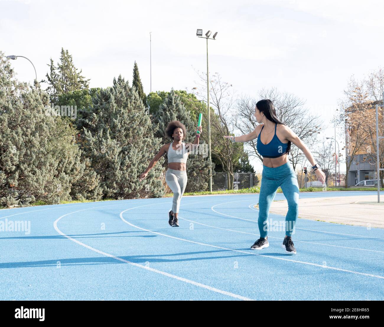 Fit multiracial female athletes passing baton while running along track ...