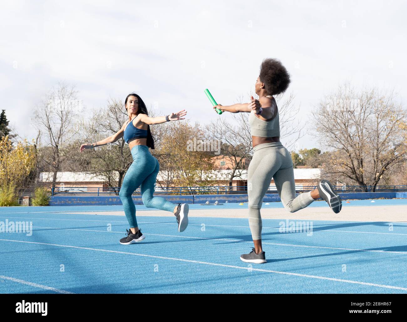 Fit multiracial female athletes passing baton while running along track ...