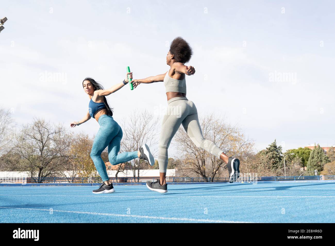 Fit multiracial female athletes passing baton while running along track ...