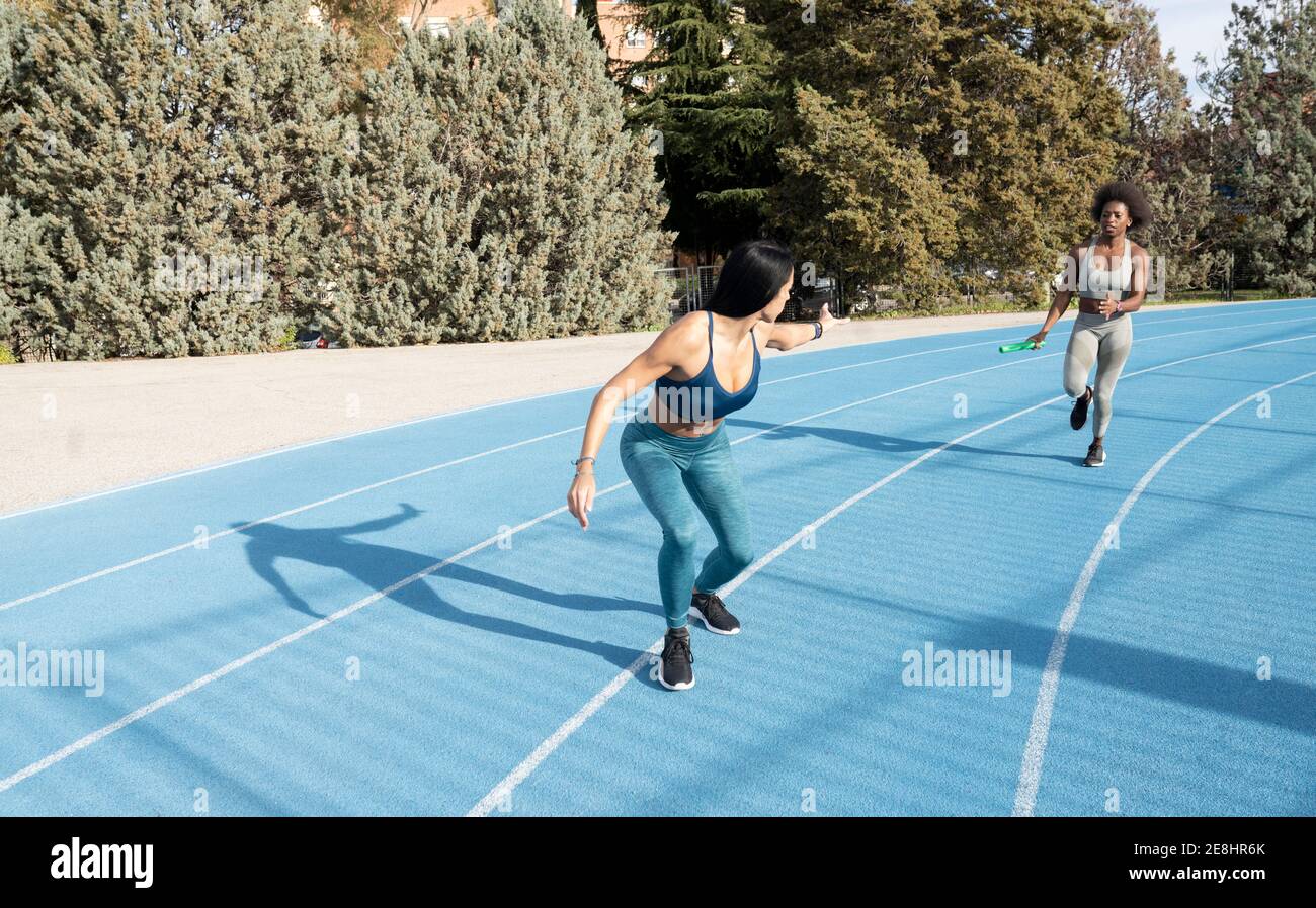 Fit multiracial female athletes passing baton while running along track ...