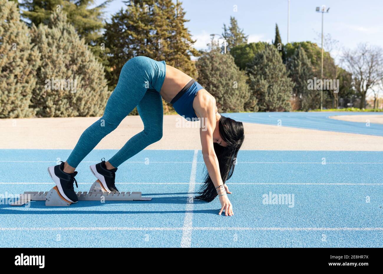 Side view of sportsWoman standing in starting blocks in crouch start ...