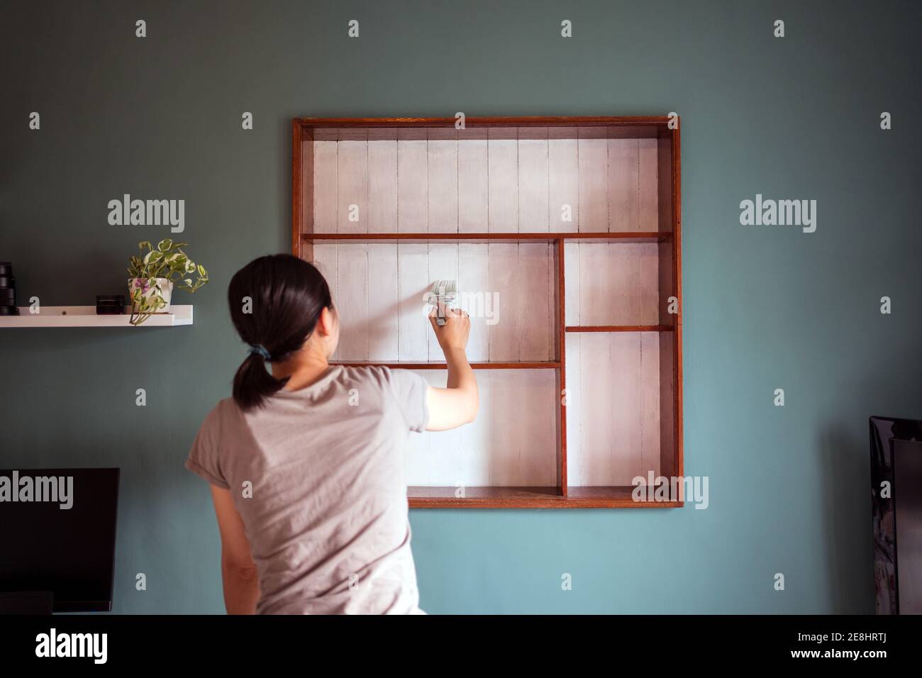 Back view ethnic female with paintbrush painting wooden shelves in ...