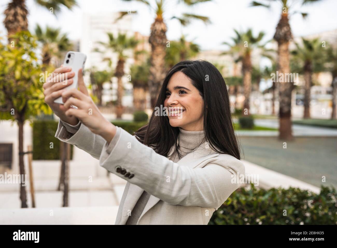 Smiling charming female taking selfie on smartphone while standing in ...