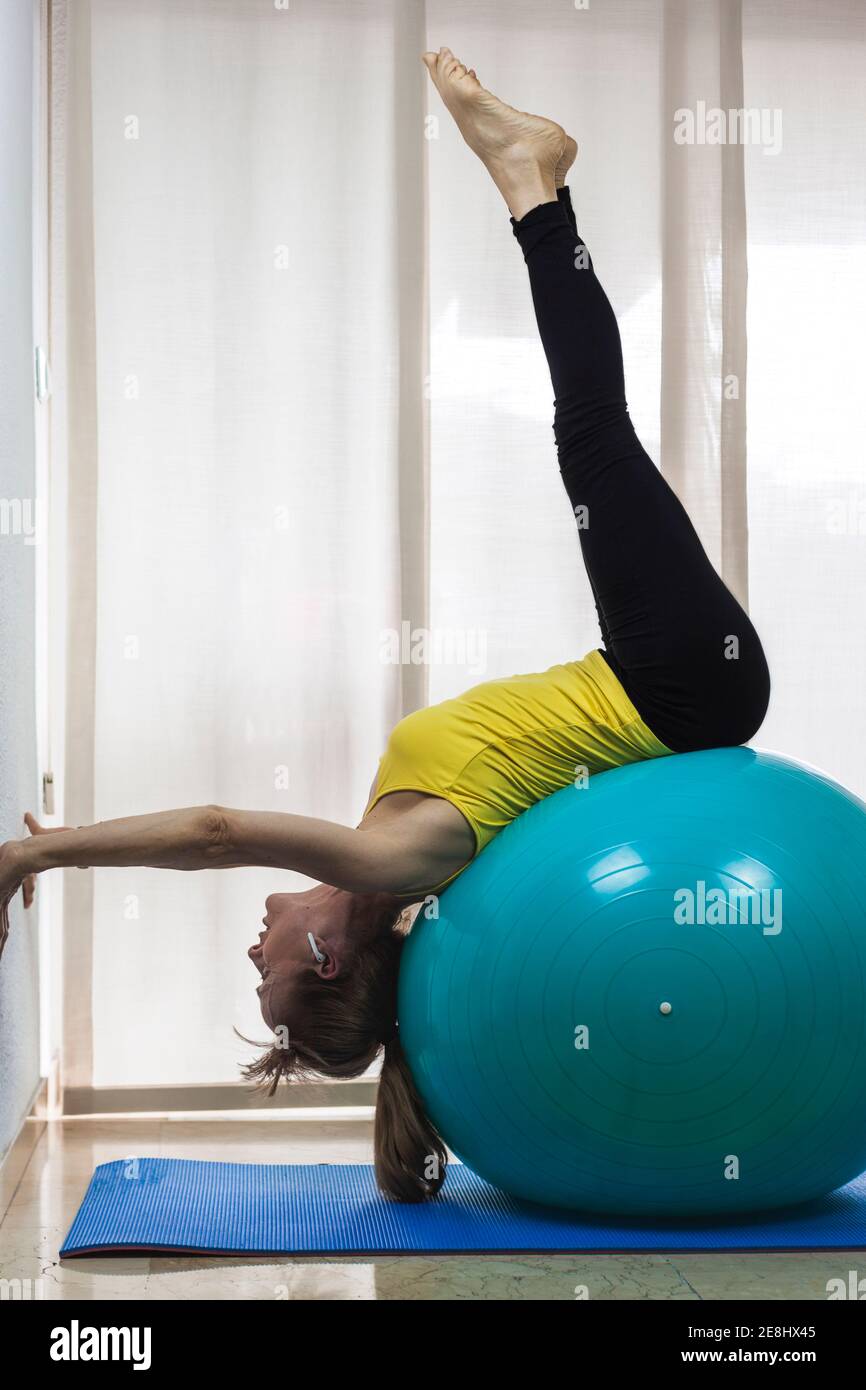 Side view fit female in activewear stretching back muscles on big yoga ...