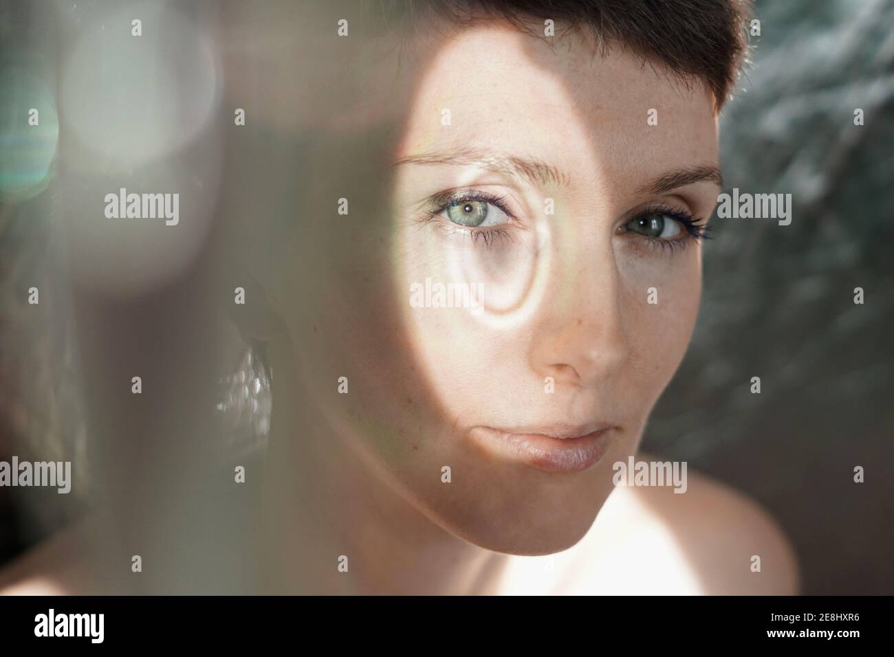 Through glass of peaceful adult lady with short hair looking at camera ...