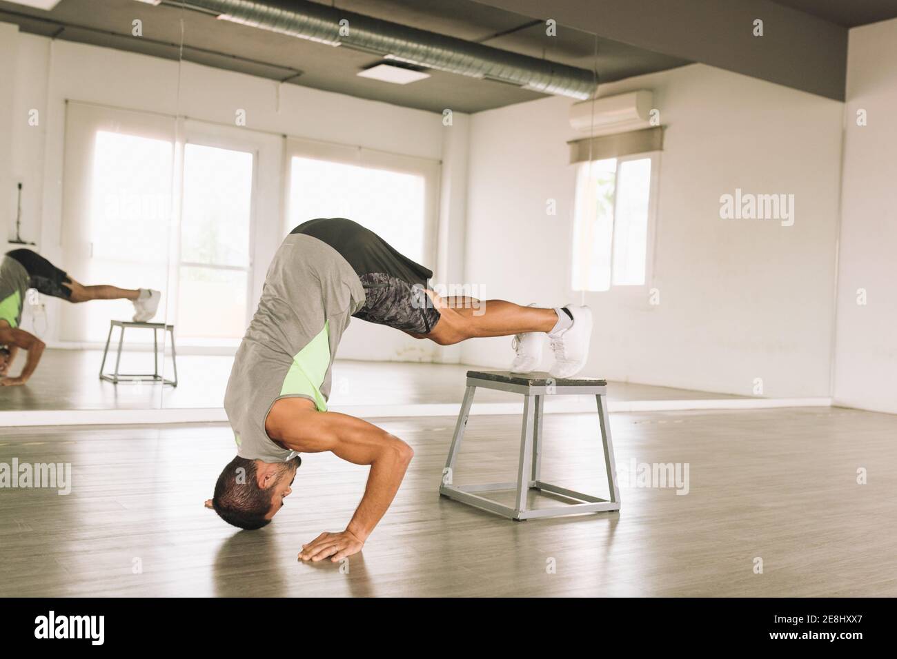 Side view of young muscular male gymnast doing Pike Push Ups with legs ...