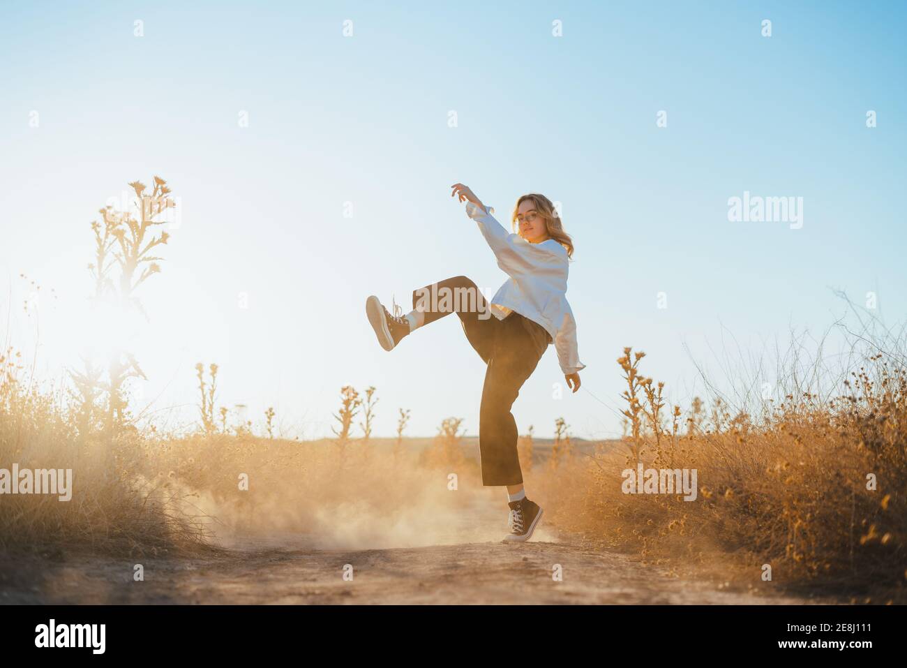 Side view of active young lady in trendy outfit dancing in dry fiends ...