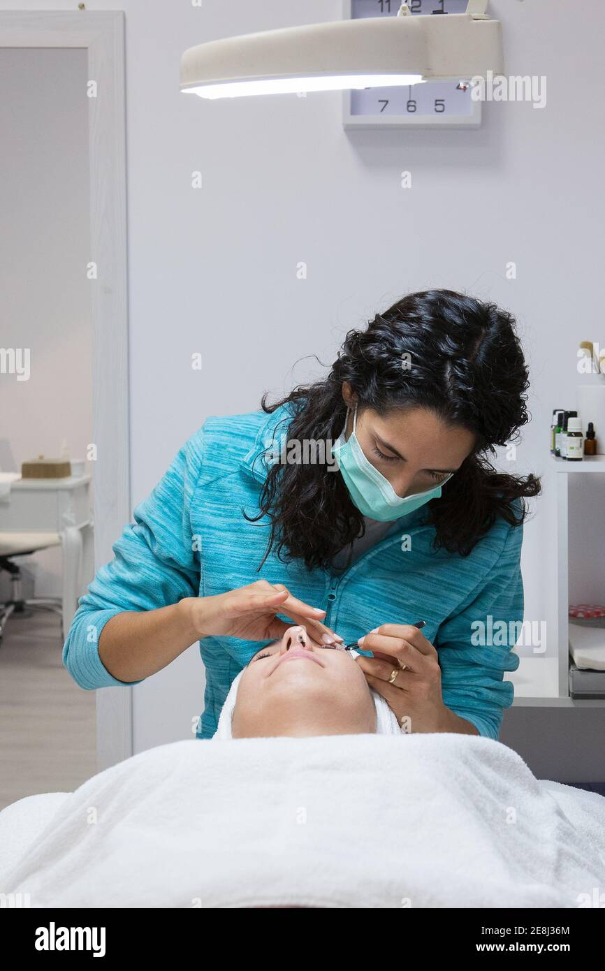 Crop anonymous beautician in mask treating adult Woman with closed eyes ...