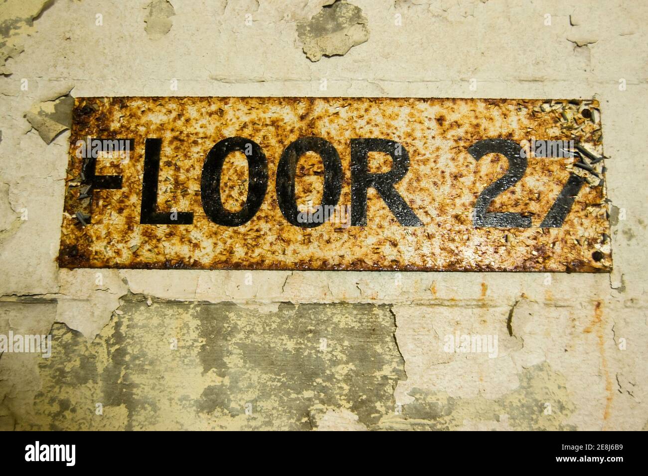 Rusting enamlled metal sign for Floor 27 on a wall with peeling paint ...