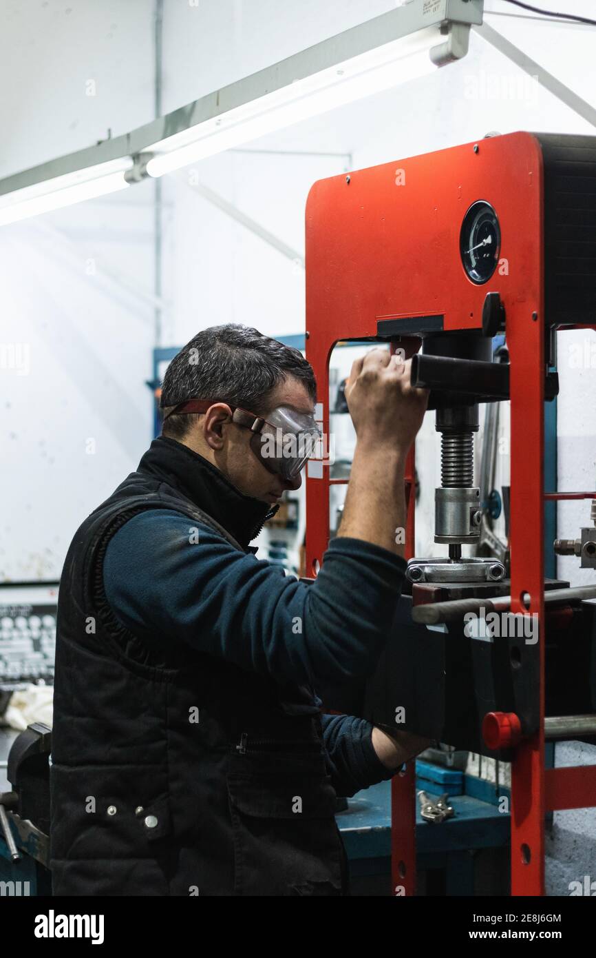 Side view of male auto mechanic in protective goggles using hydraulic ...