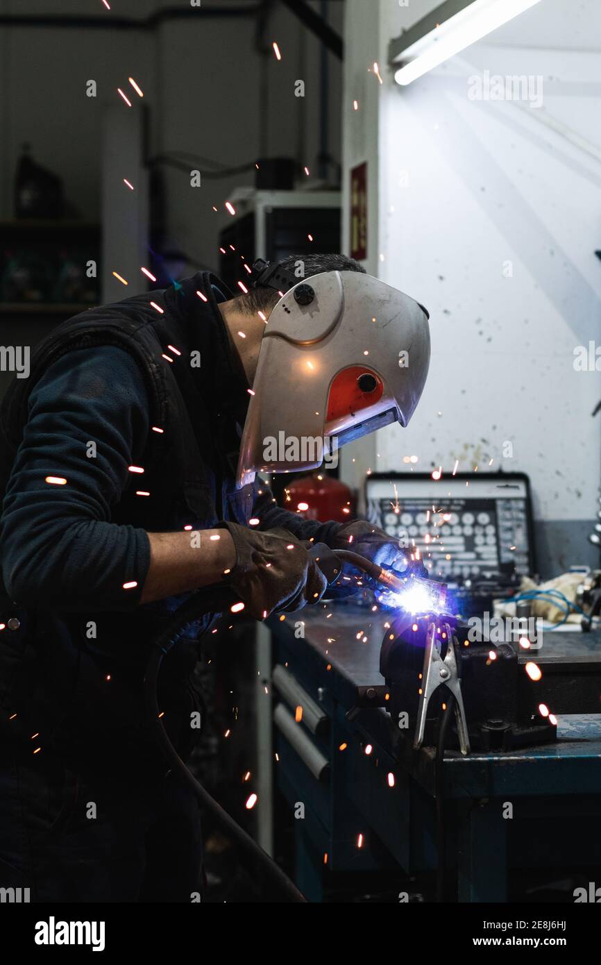 Side view of unrecognizable repairman in protective helmet using torch ...