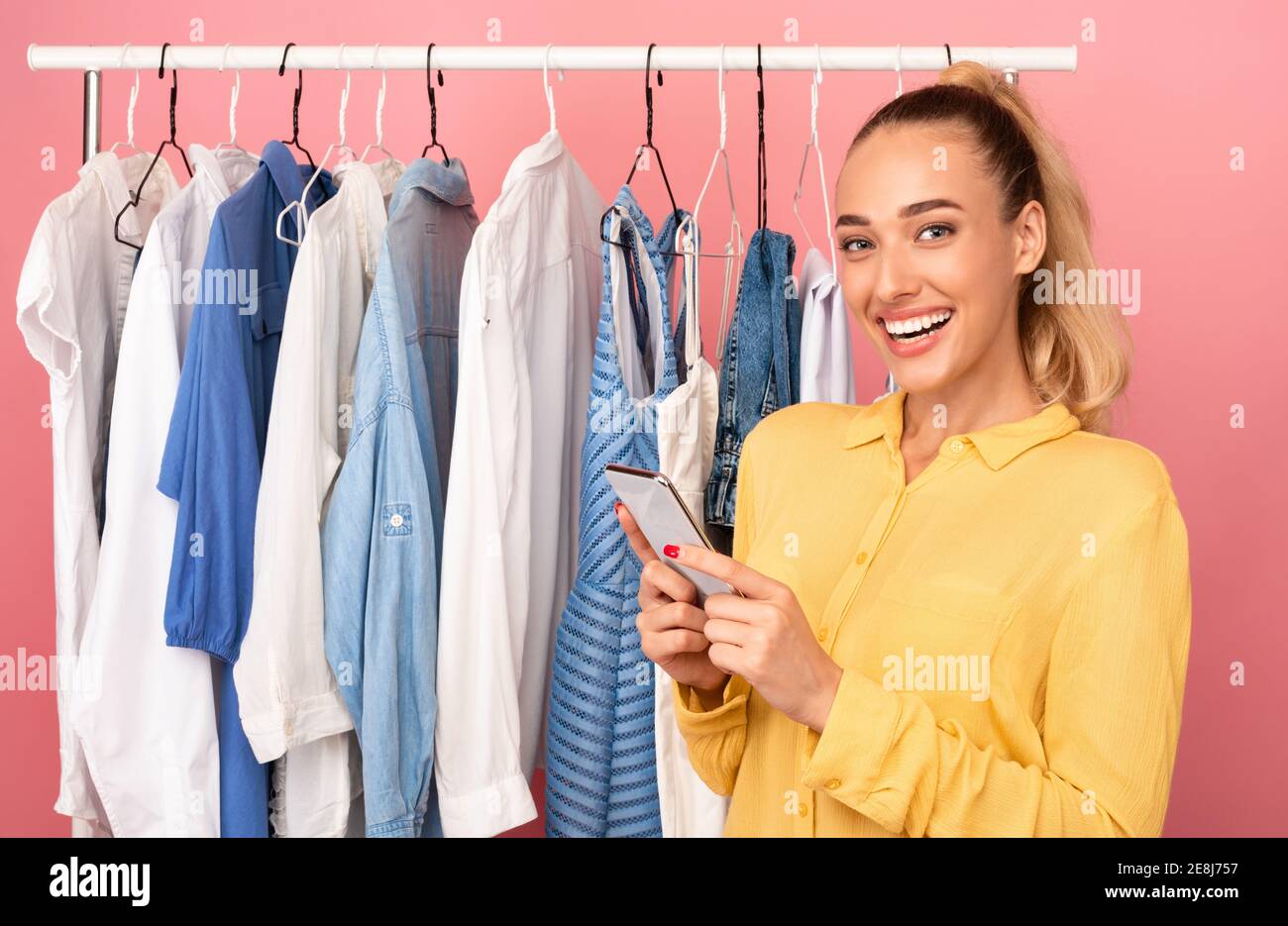 Smiling lady holding phone standing near rack with clothing Stock Photo ...