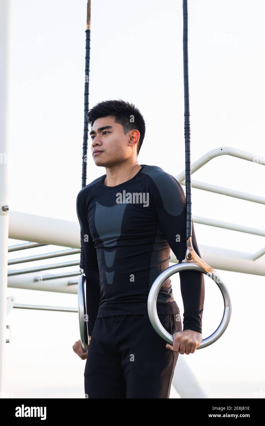 Low angle of young Asian sportsman in black activewear hanging on ...