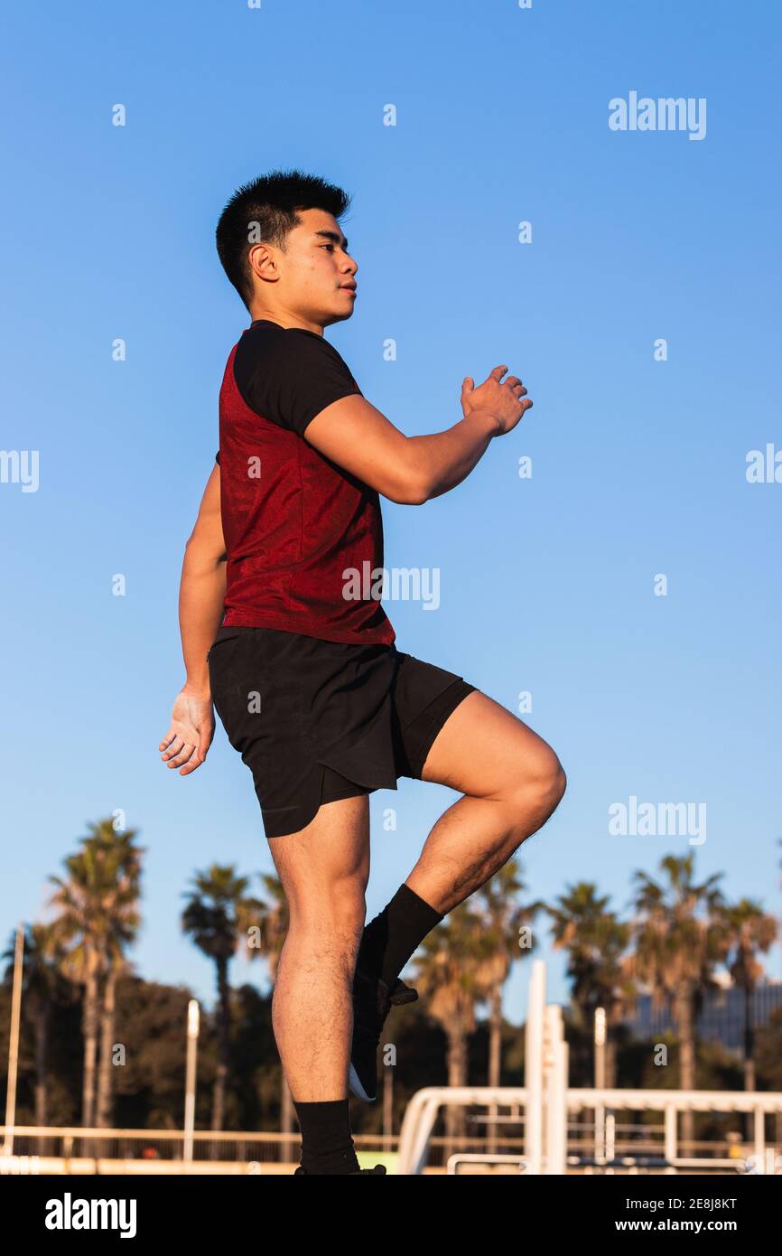 Side view of determined young Asian male in sportswear performing step ...