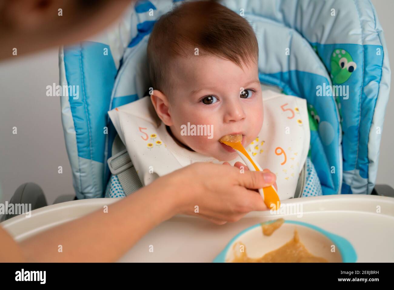 Adorable happy kid wearing bib sitting in stroller and getting fed with ...