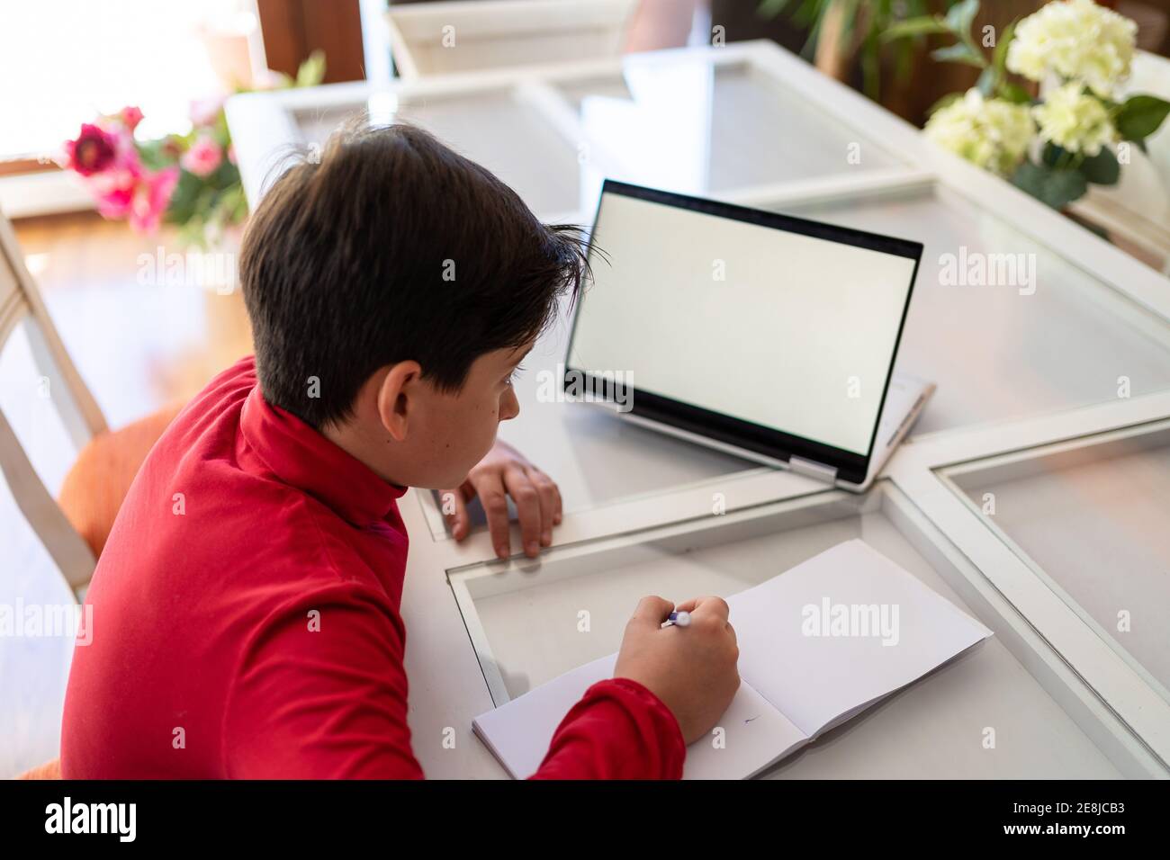 High angle side view of smart schoolboy sitting at table with laptop ...