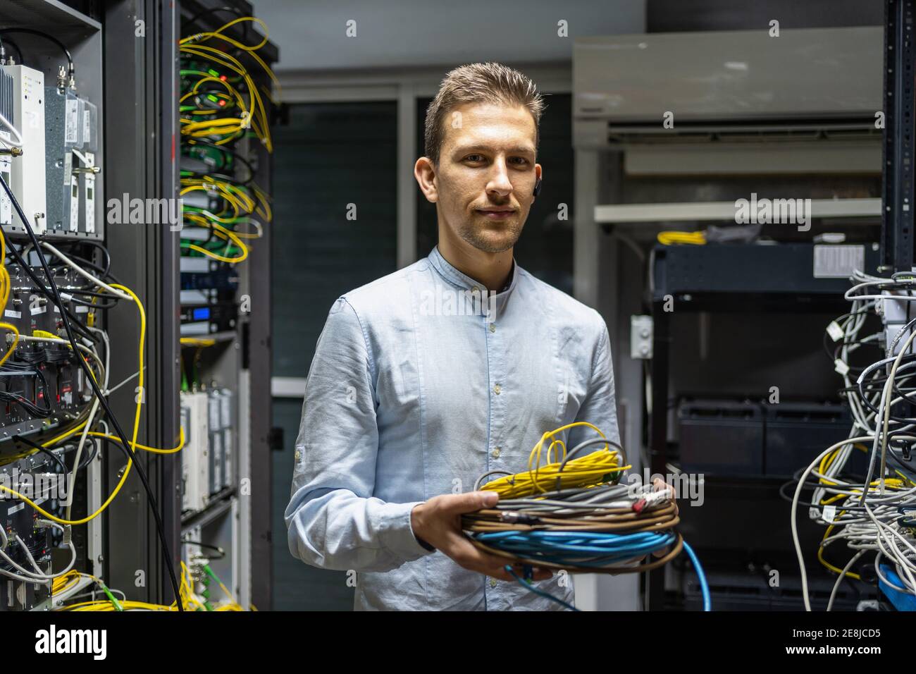 Smiling man in wireless headset standing with cables in network server ...