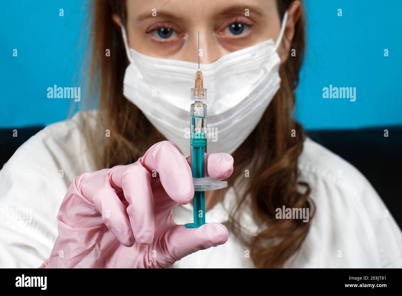 Young nurse holding medical syringe with needle wearing glove and face ...