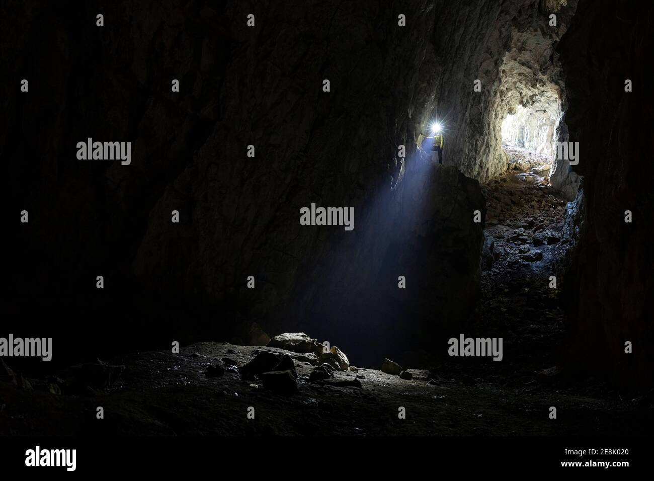 Woman with a headlamp standing on a large rock in a cave, light coming ...