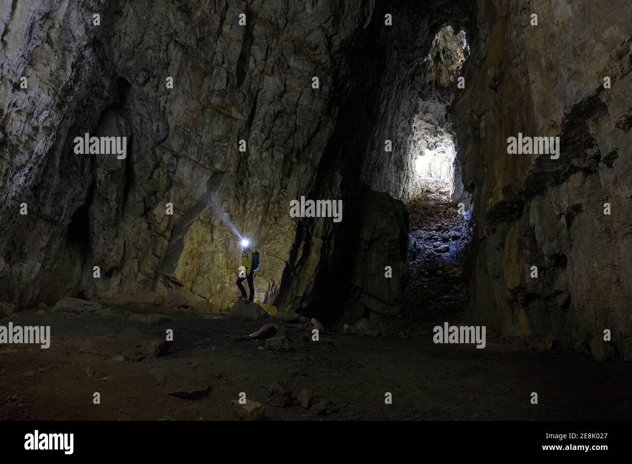 Woman with a headlamp standing on a large rock in a cave, light coming ...