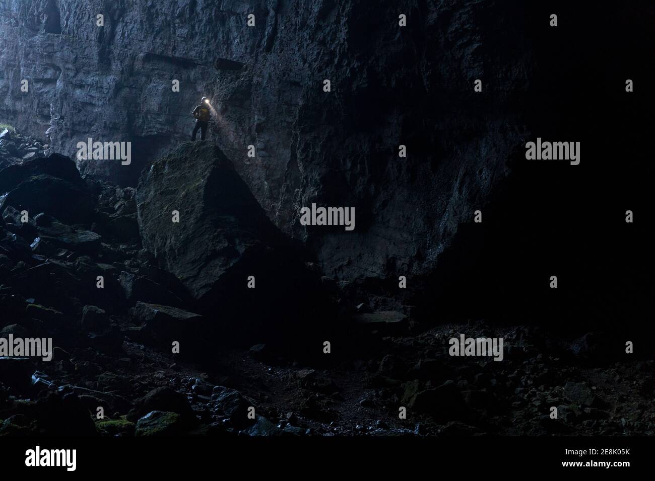Woman with a headlamp standing on a large rock in a cave, light coming ...