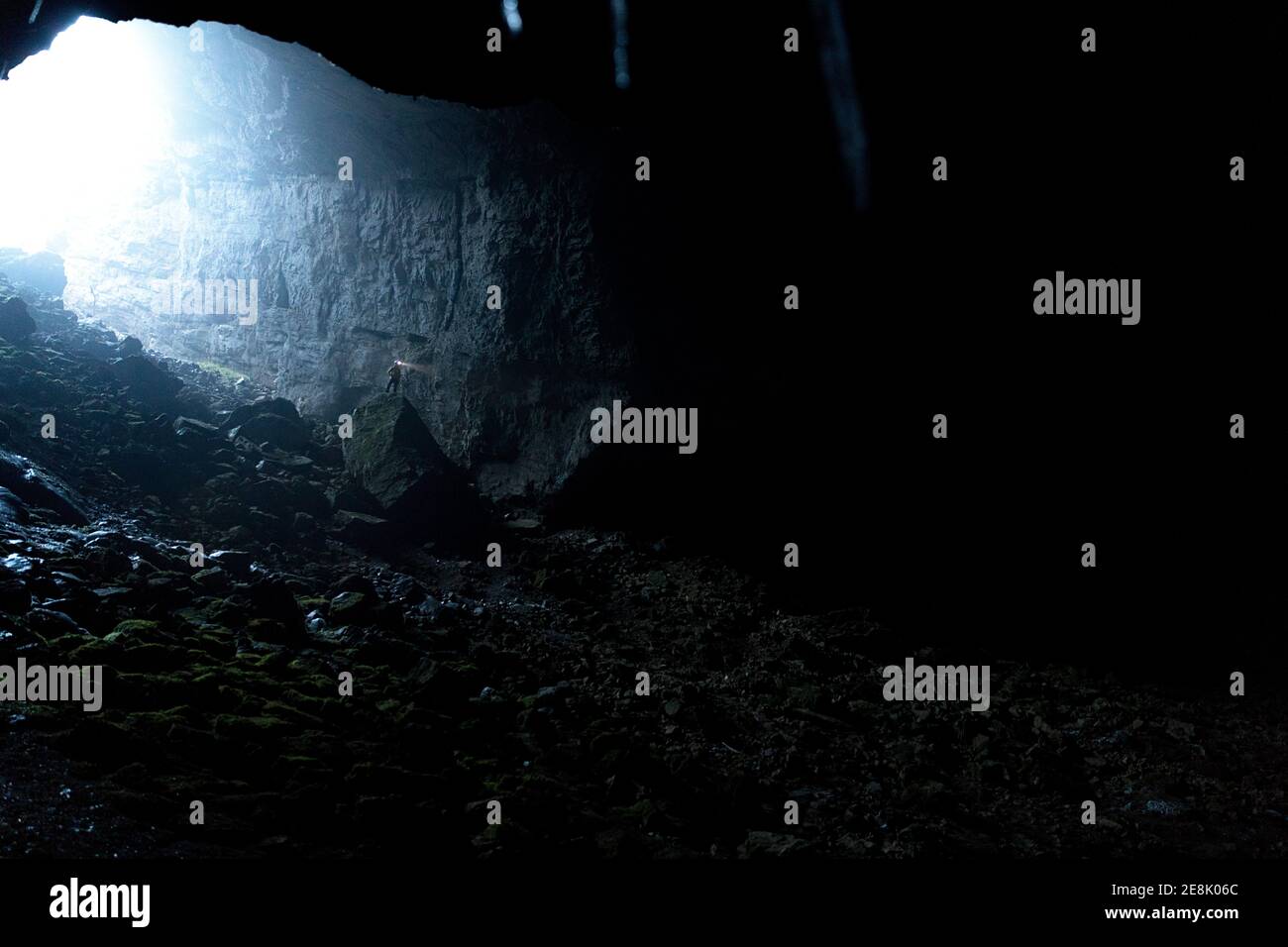 Woman with a headlamp standing on a large rock in a cave, light coming ...