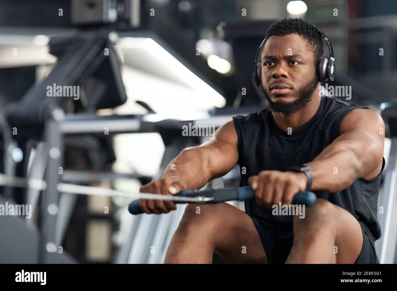 Handsome sportsman training body on modern rowing exerciser in gym ...