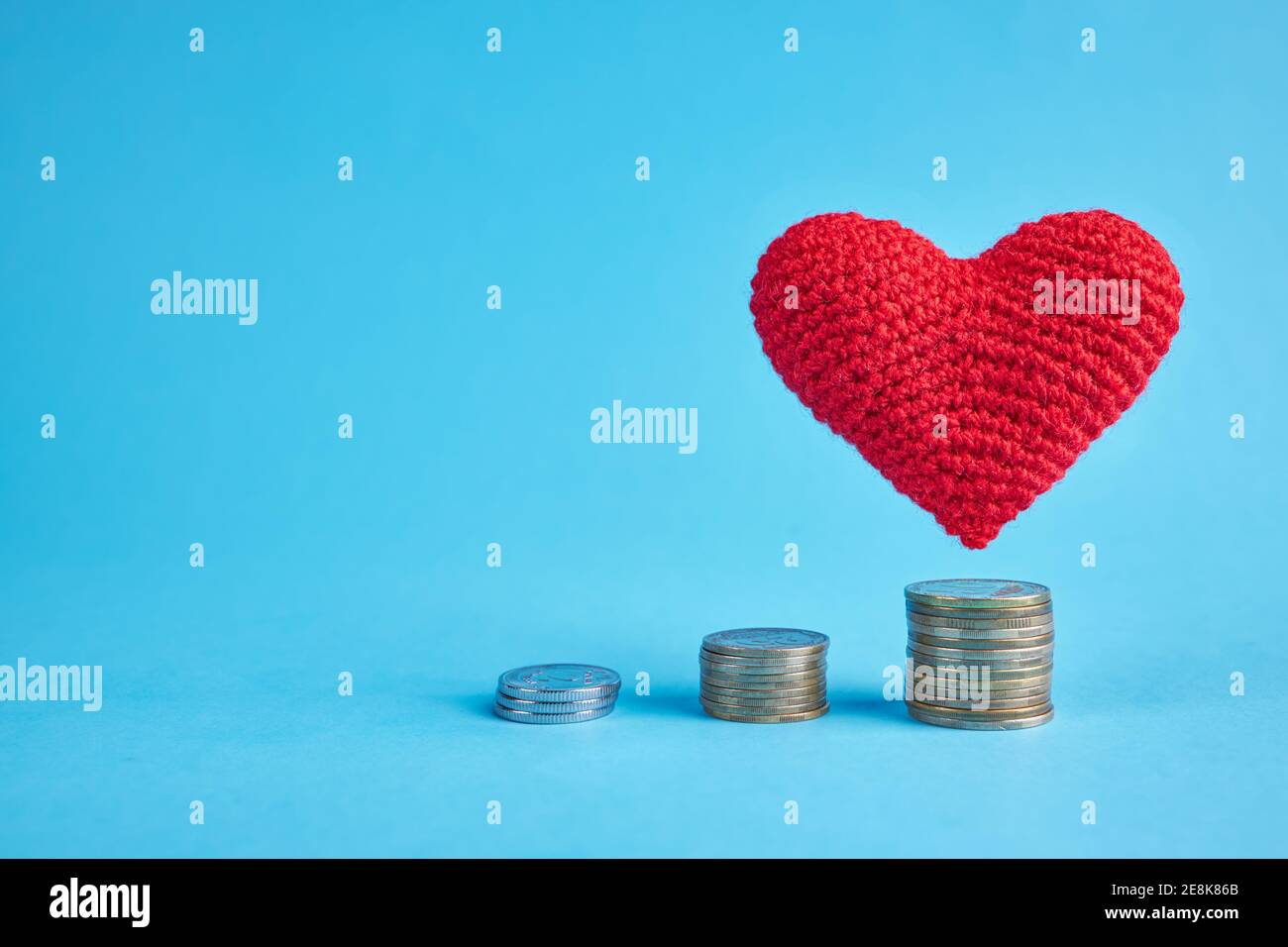 Red heart flying under coin stacks over blue background. copy space ...