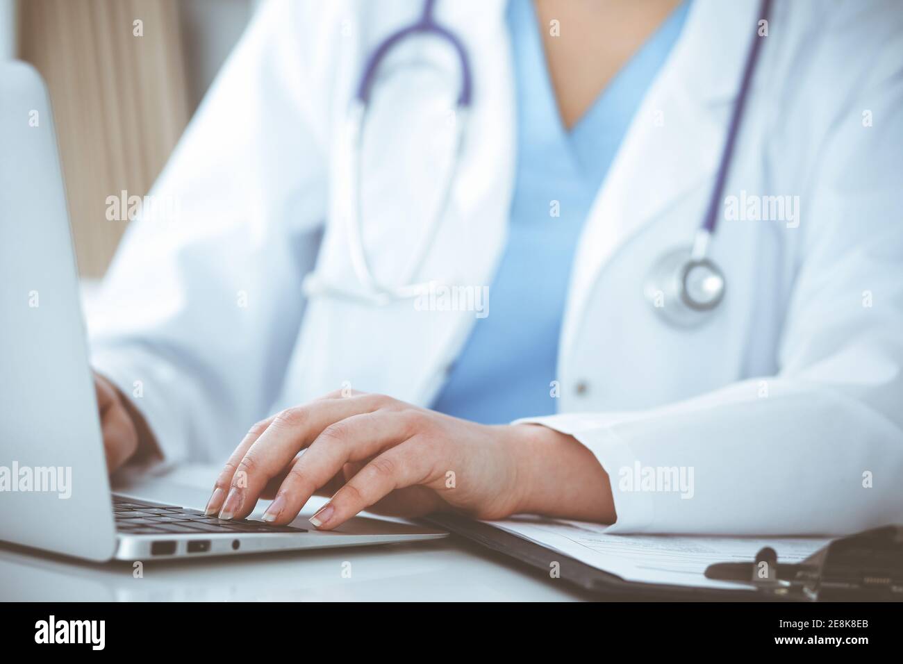 Unknown woman-doctor typing on laptop computer while sitting at the ...
