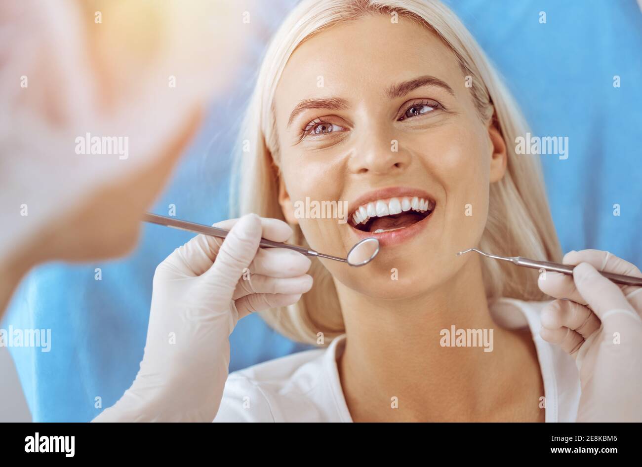 Smiling blonde woman examined by dentist at sunny dental clinic ...