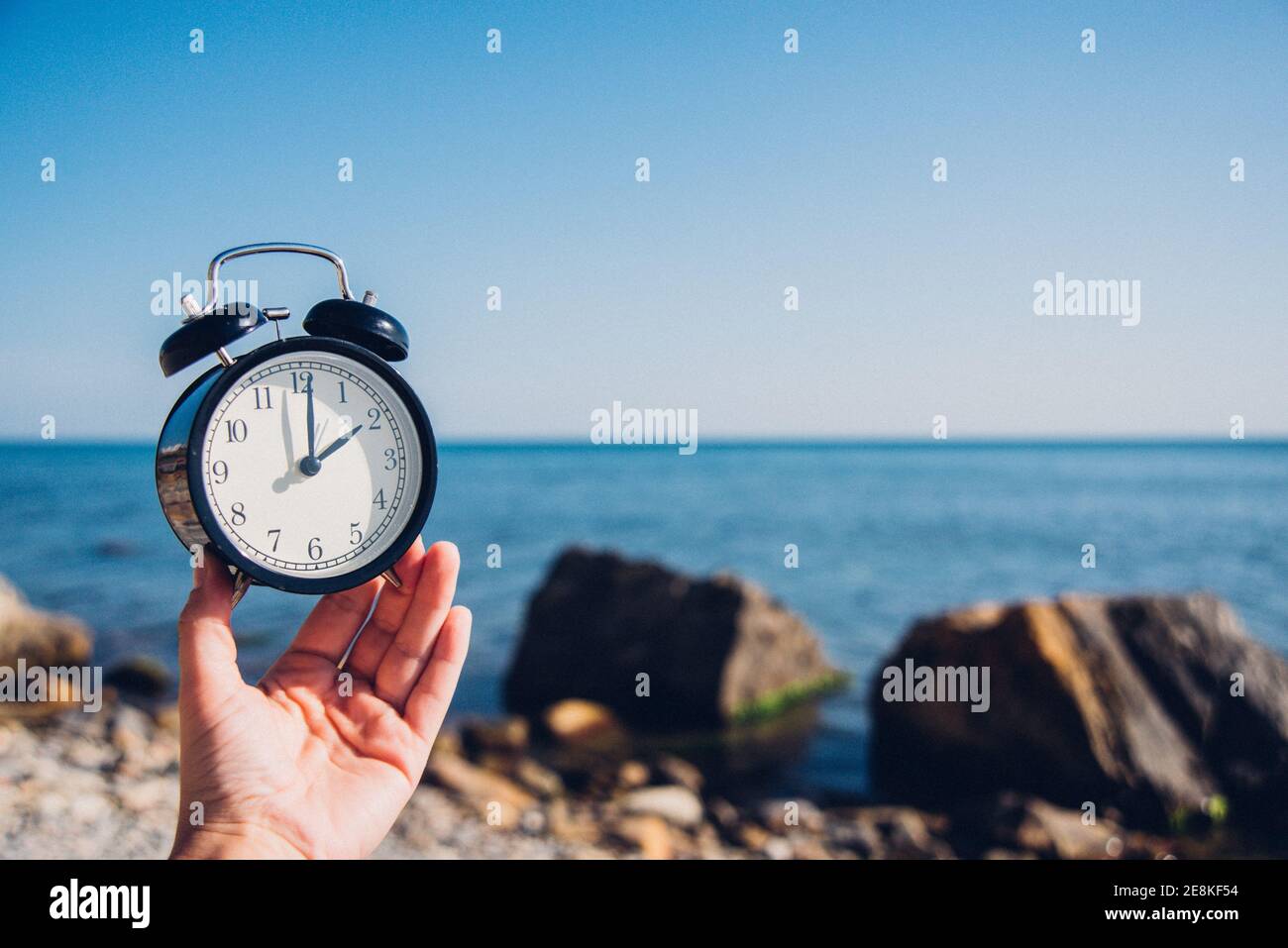 Hand hold watch on beach background.Alarm clock on sea and sand ...