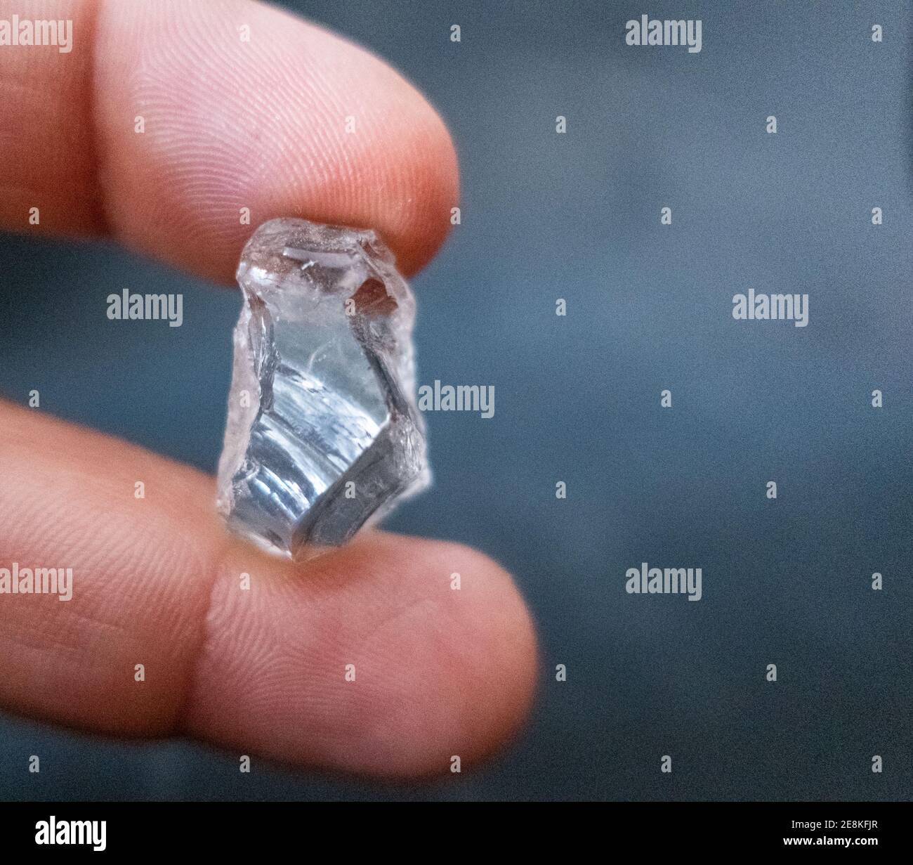 A closeup shot of a hand holding a piece of broken glass on a blue ...