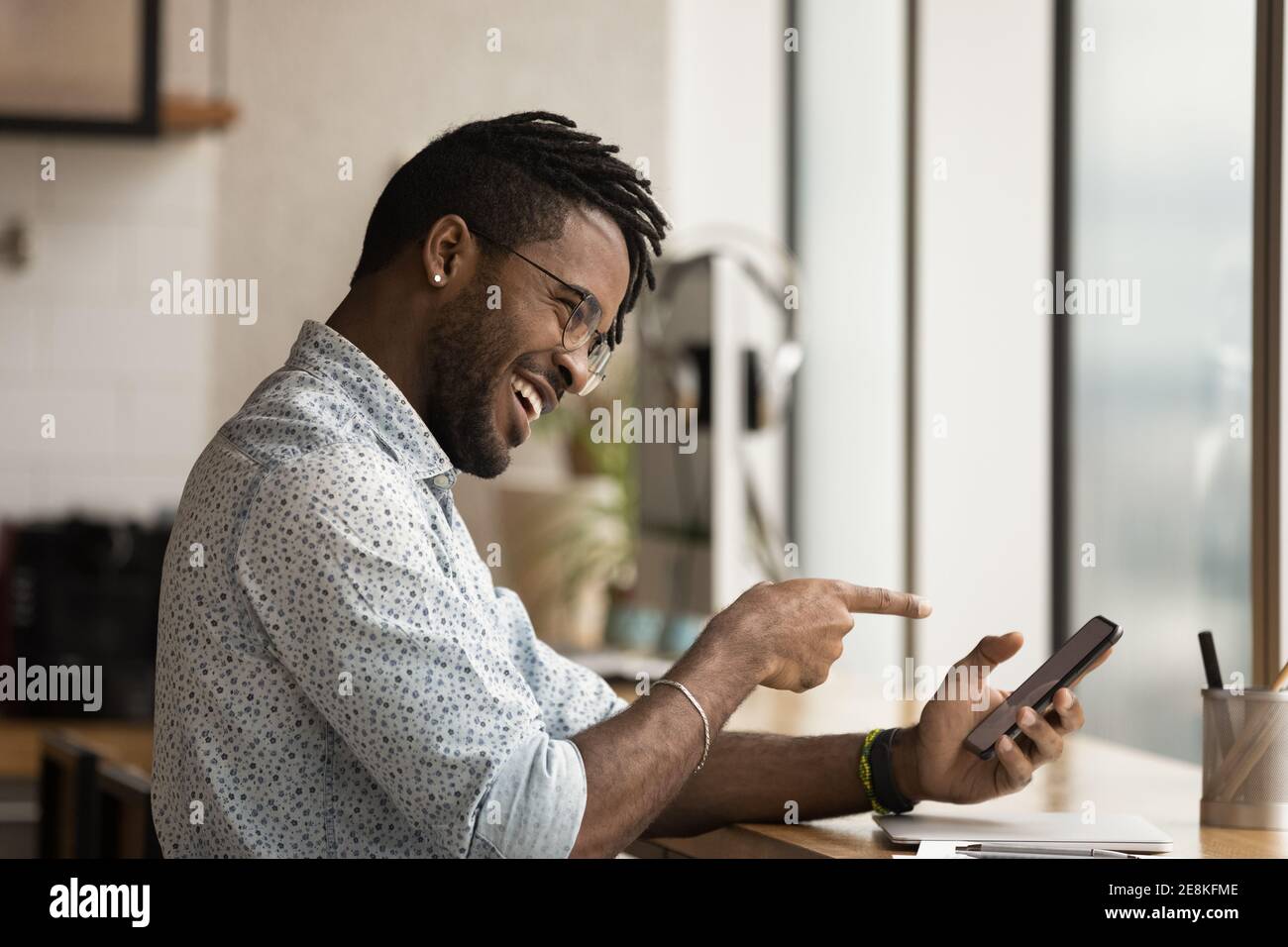 Laughing african guy pointing at phone screen chatting with friend ...