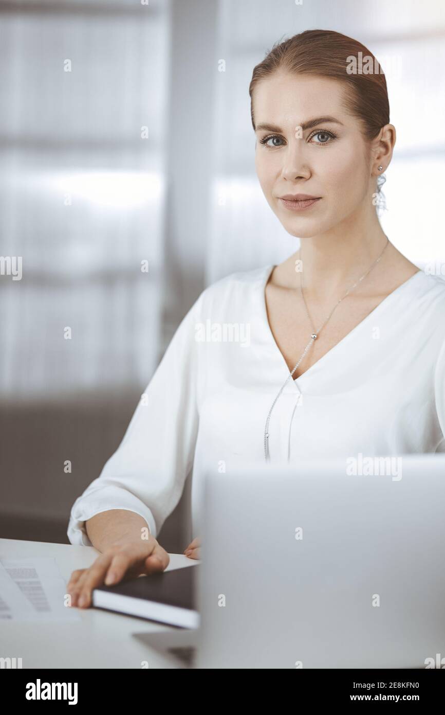 Businesswoman sitting and looking at camera in sunny office Stock Photo ...