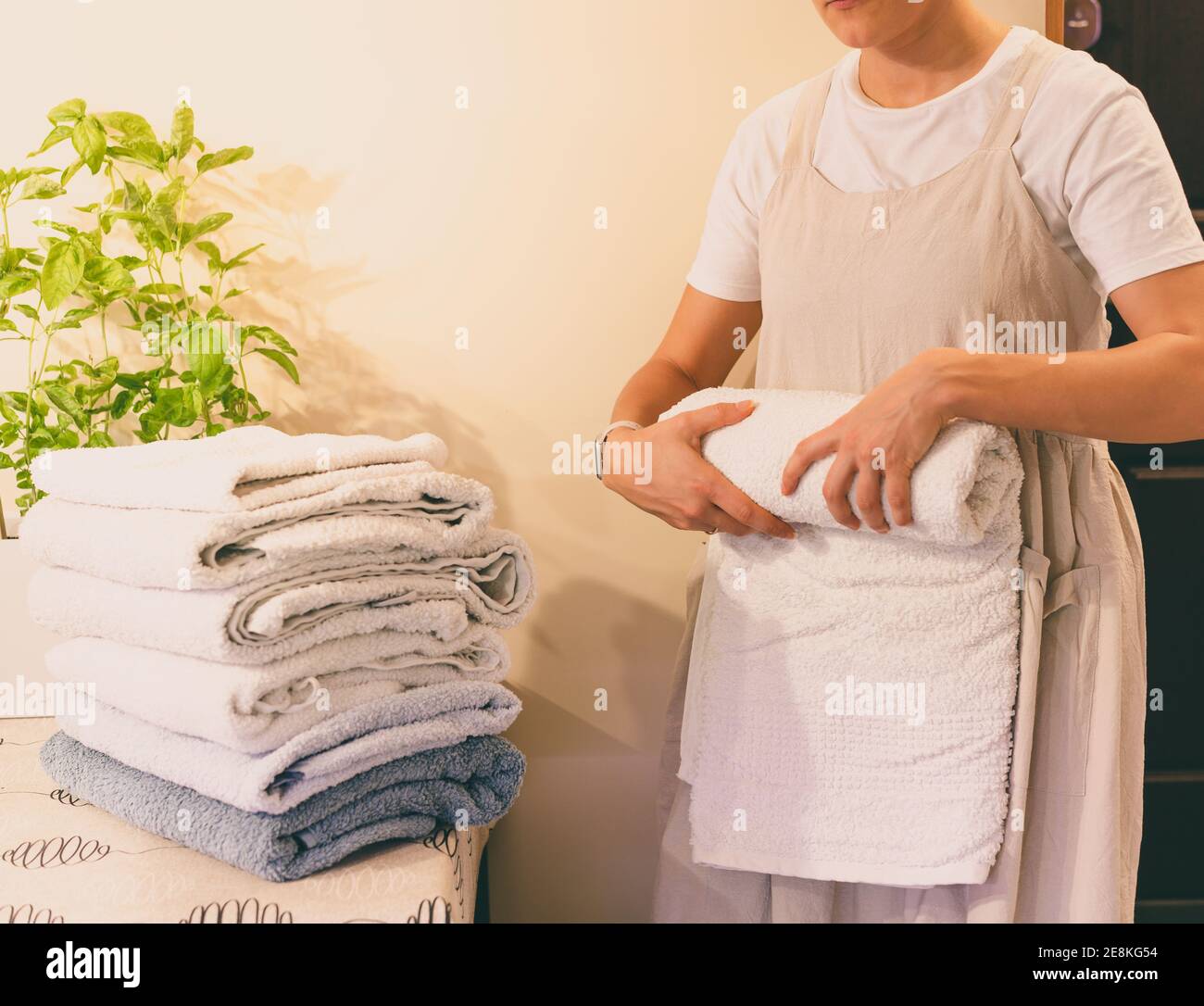 Woman twisting up a roll of clean white bath towels on light background ...